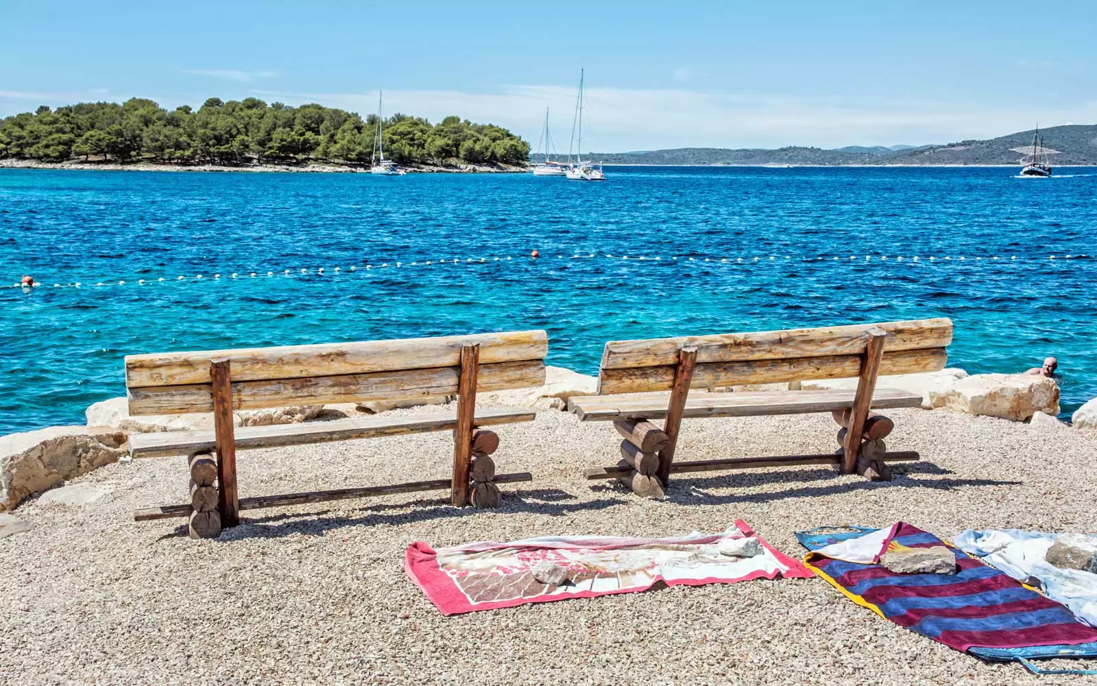 Bancos de madera y toallas en la playa, Solta, Croacia