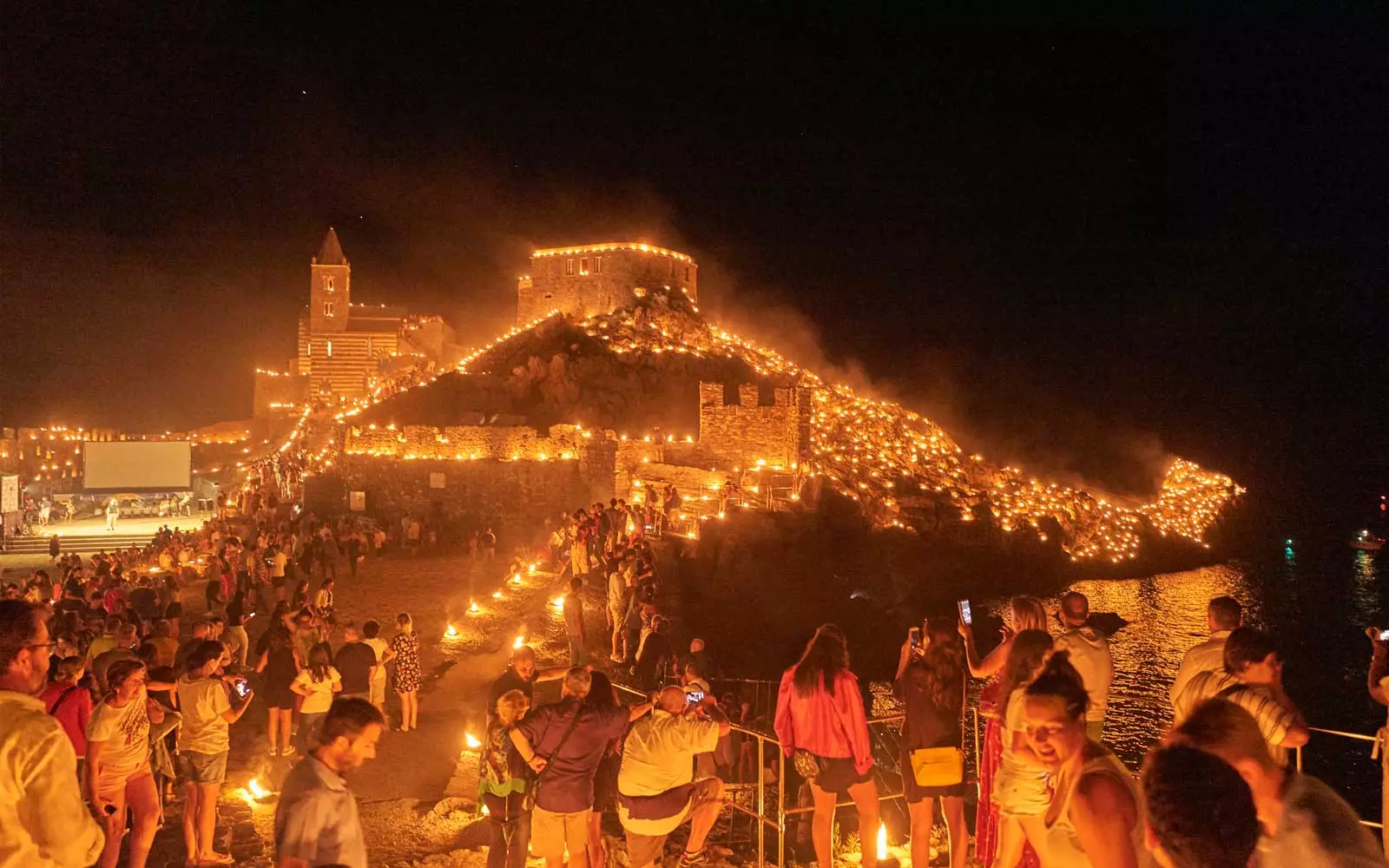 17/08/2019 Porto Venere, Italio. Homoj staras ĉe la rando de la malnova urbo, ĉe la maro, kun kandeloj lumigitaj ĉie, por la festadoj de Madono Bianca.