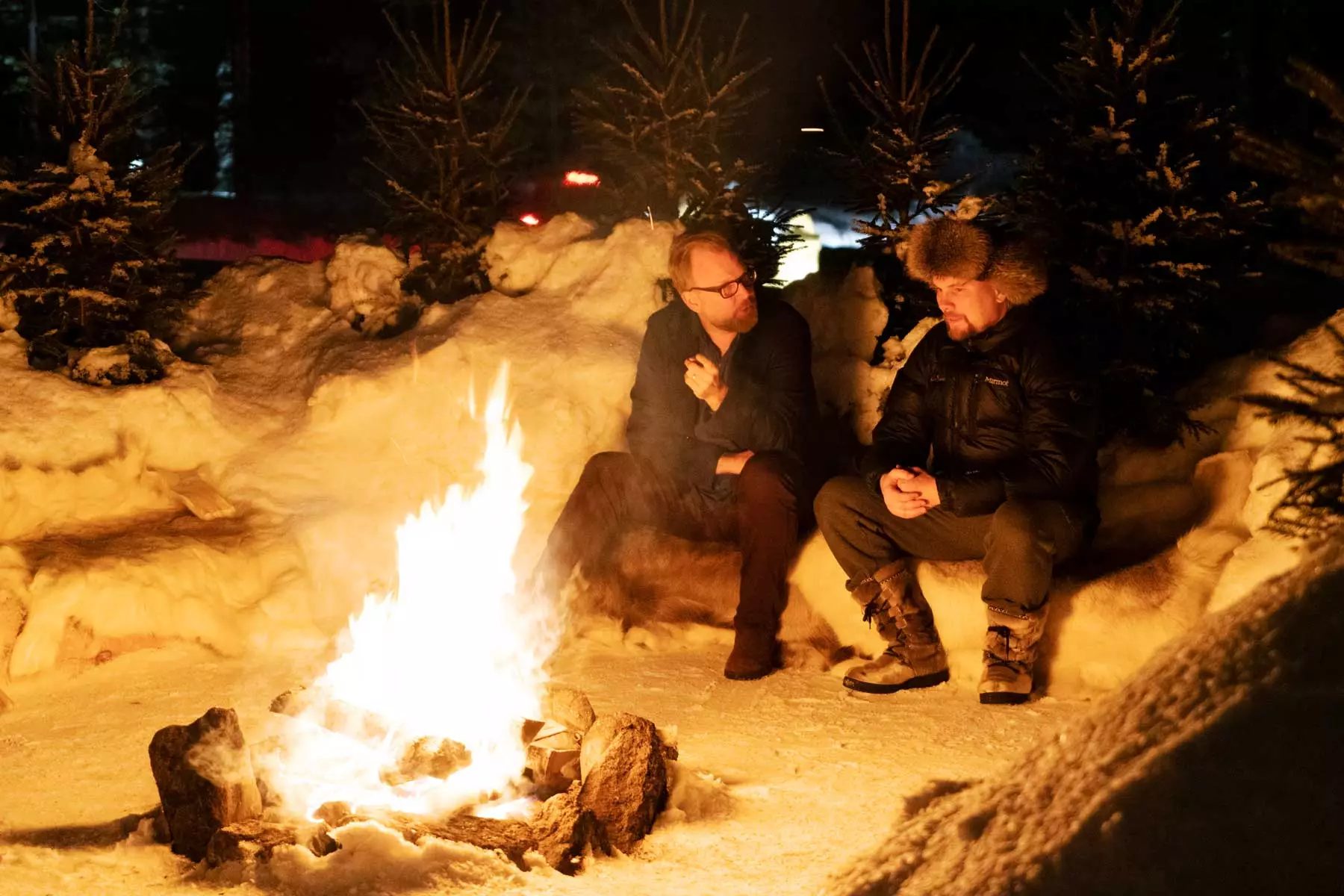 Twee mannen, zittend op een sneeuwbank, praten naast een vuurplaats in Finland