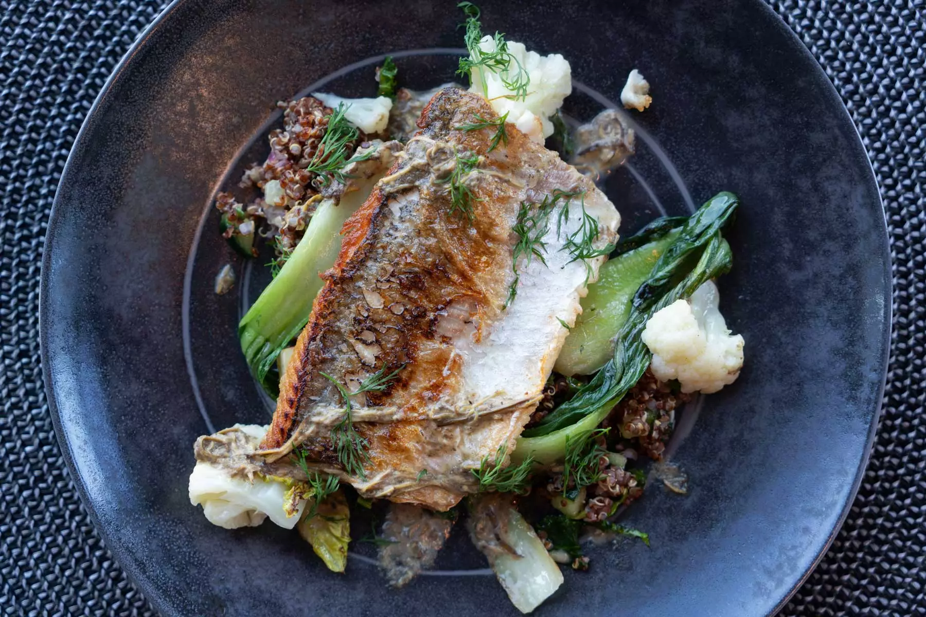 Schotel van witvis met quinoa en boy chow op een houtskoolkleurig bord bij Octola lodge in Finland