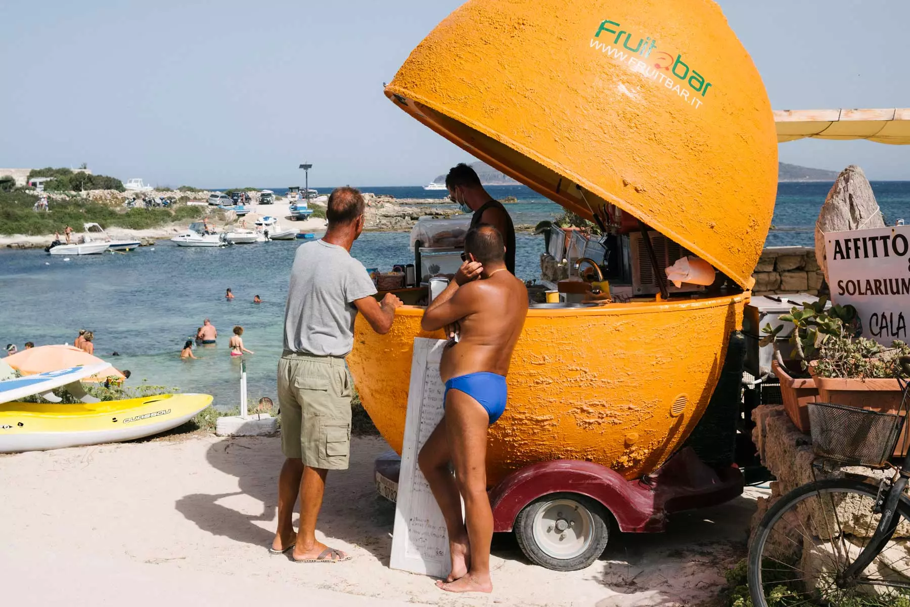 Opalonych mężczyzn stojących przy barze z sokami w kształcie pomarańczy na wyspie Favignana