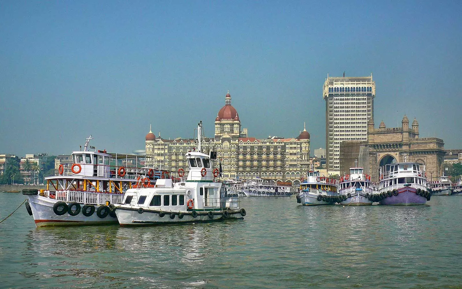 मुंबई, महाराष्ट्र, भारतातील पार्श्वभूमीत गेट ऑफ इंडिया, ताजमहाल पॅलेस आणि टॉवरसह वेलिंग्टन हार्बर (पूर्वीचा अपोलो बंदर) चे विहंगम दृश्य