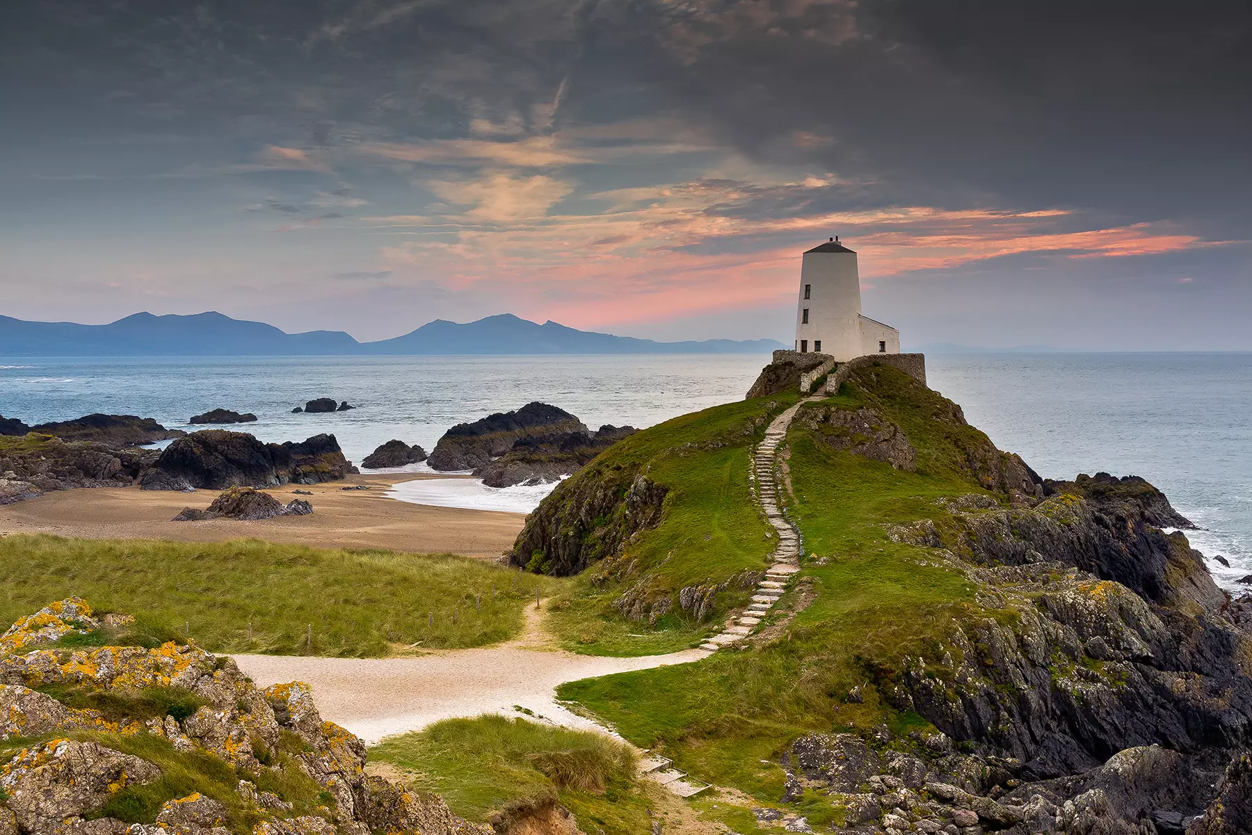 Perëndimi i diellit mbi ishullin Llanddwyn në Anglesey, me malet e Snowdonia në sfond.